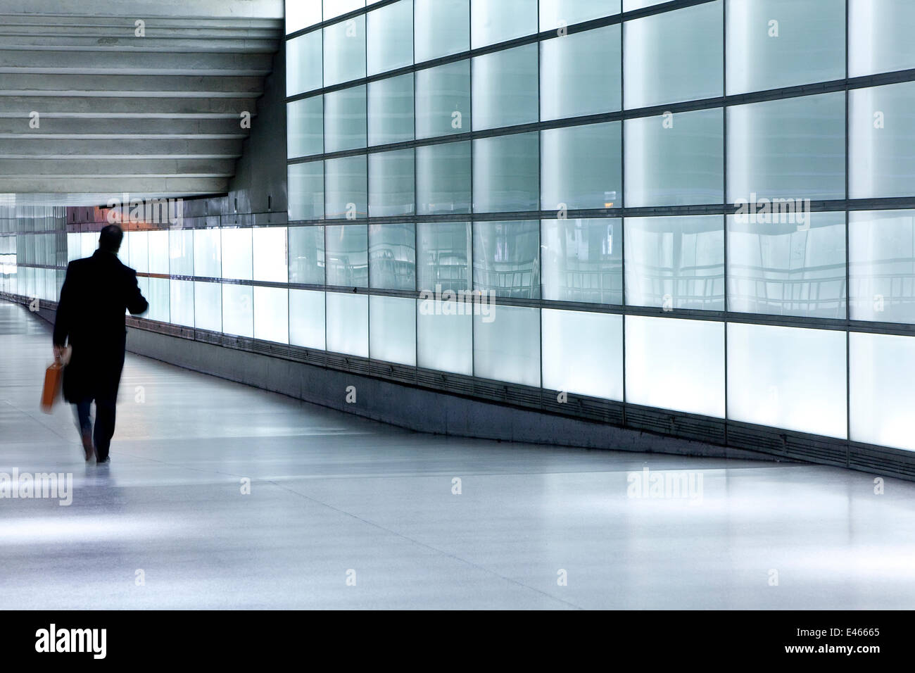 People commuting through glass walled passageway in modern building ...