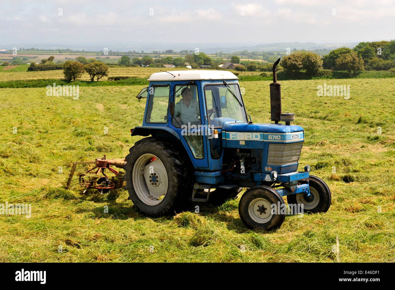 Farm tractor with "hay bob" rake turning grass to aid drying for hay or ...