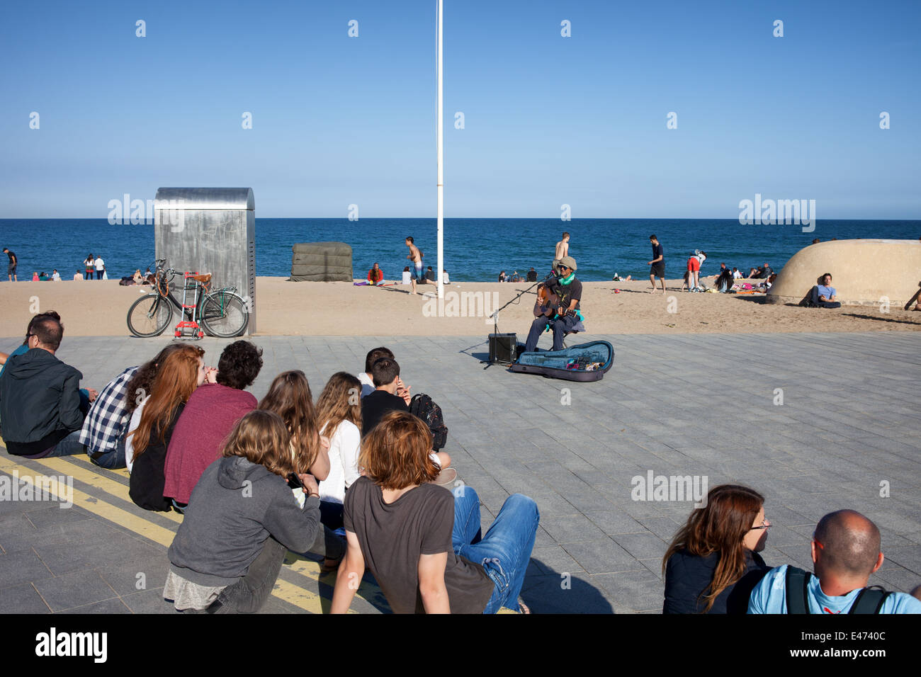 People listen to busker playing guitar on Barceloneta promenade in Barcelona, Catalonia, Spain ...