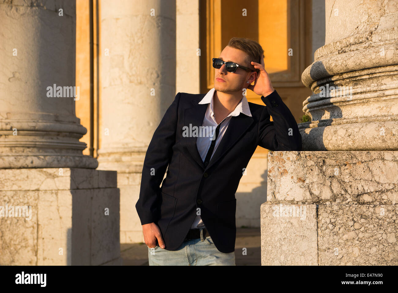 Handsome blond young man with marble columns behind him, looking away ...