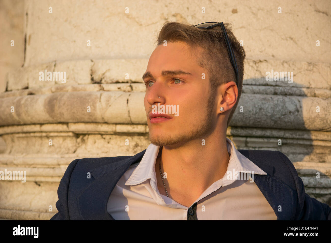 Handsome blond young man with marble columns behind him, looking away ...