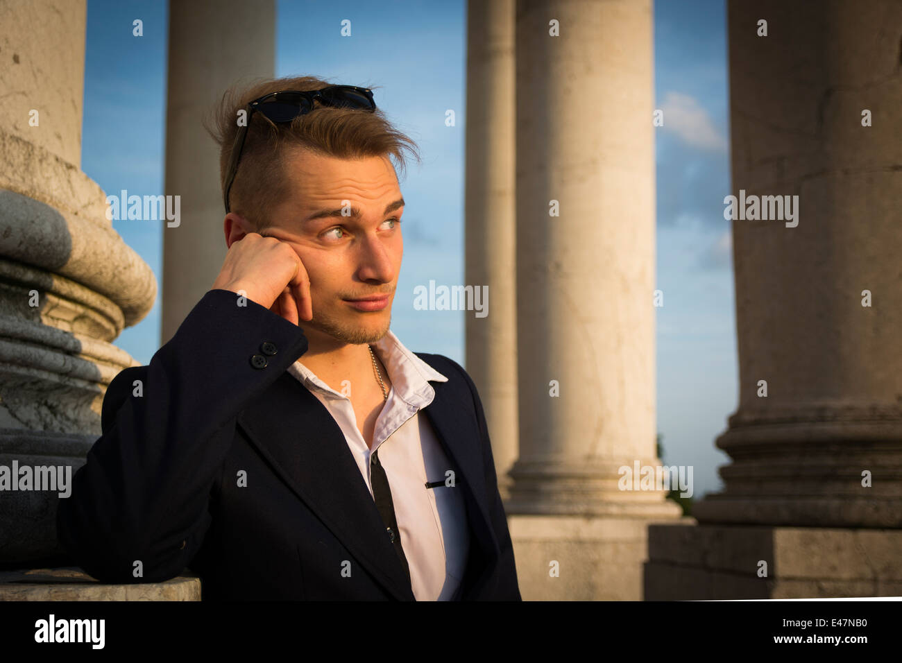 Handsome blond young man with marble columns behind him, looking away ...