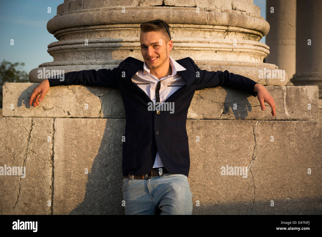 Handsome smiling blond young man with marble column behind him, looking ...