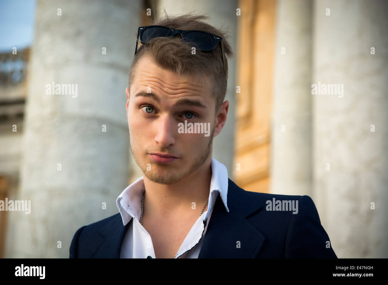 Handsome blond young man with marble columns behind him, looking at ...