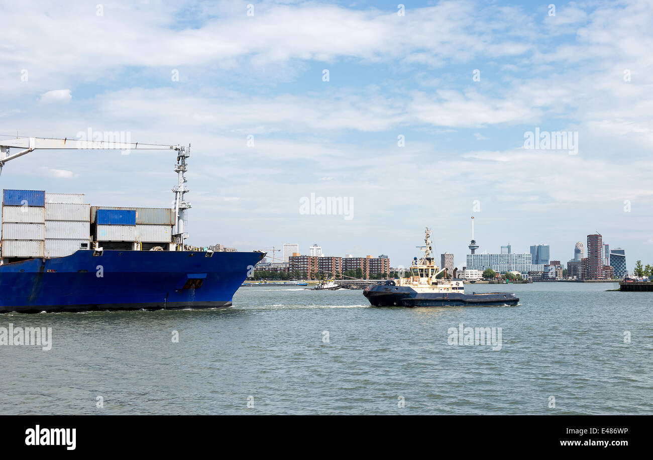 containership entering rotterdam harbor with tug and skyline as ...