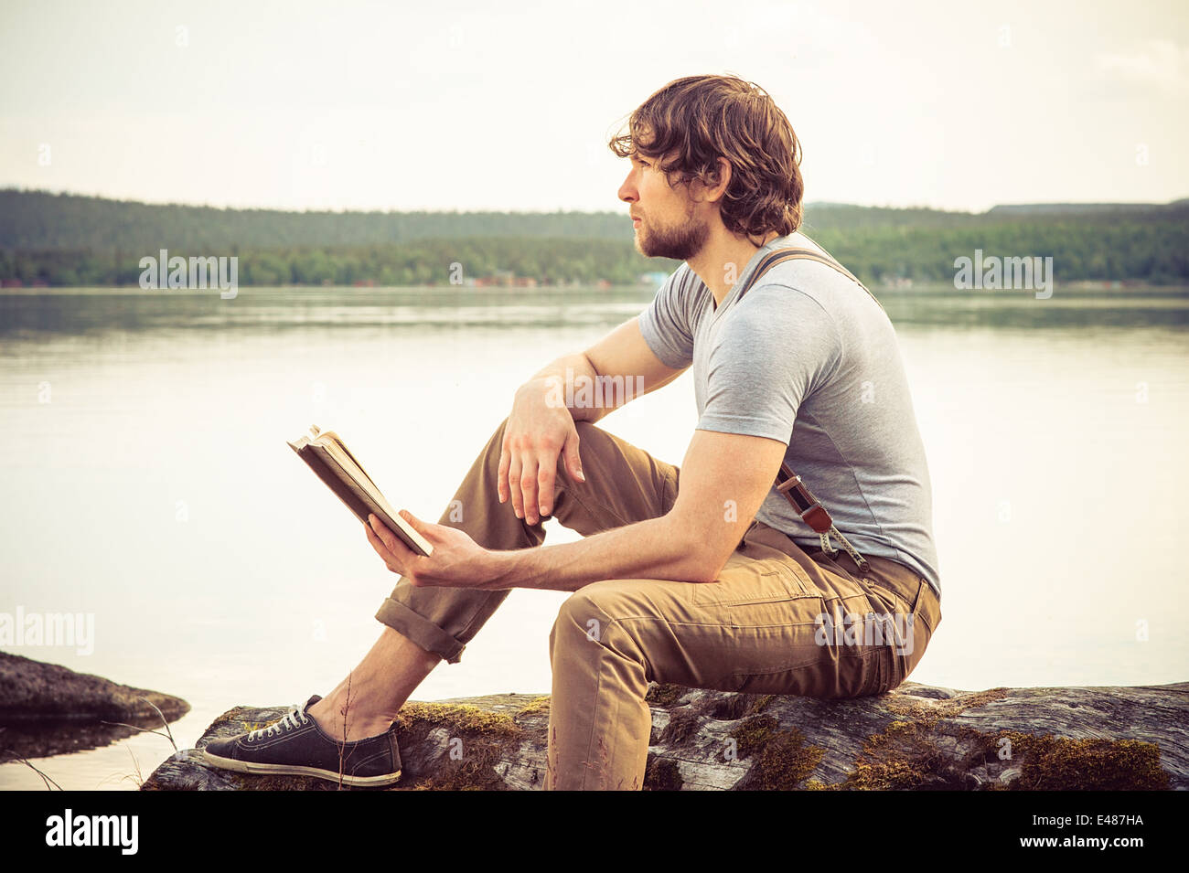 Young Man reading book outdoor with lake on background Summer vacations ...