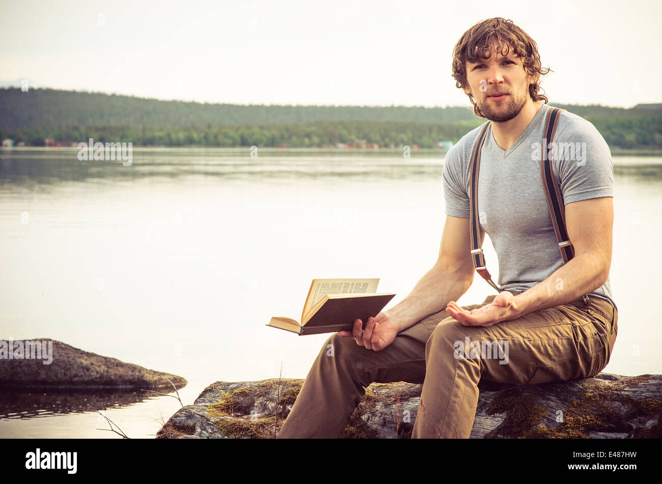 Young Man reading book outdoor with lake on background Summer vacations ...