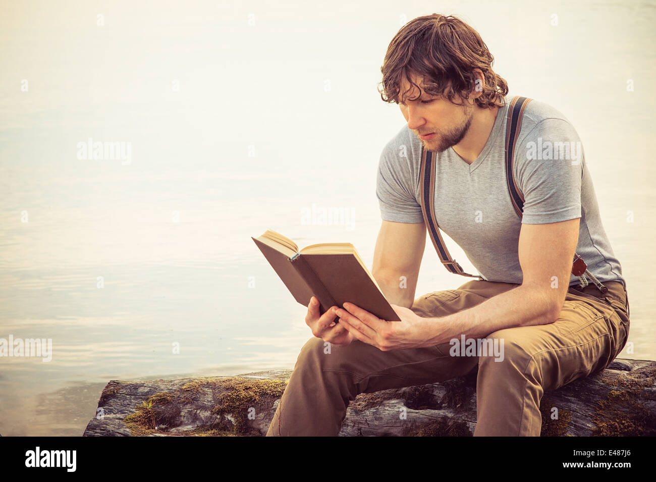 Young Man reading book outdoor with lake on background Summer vacations ...