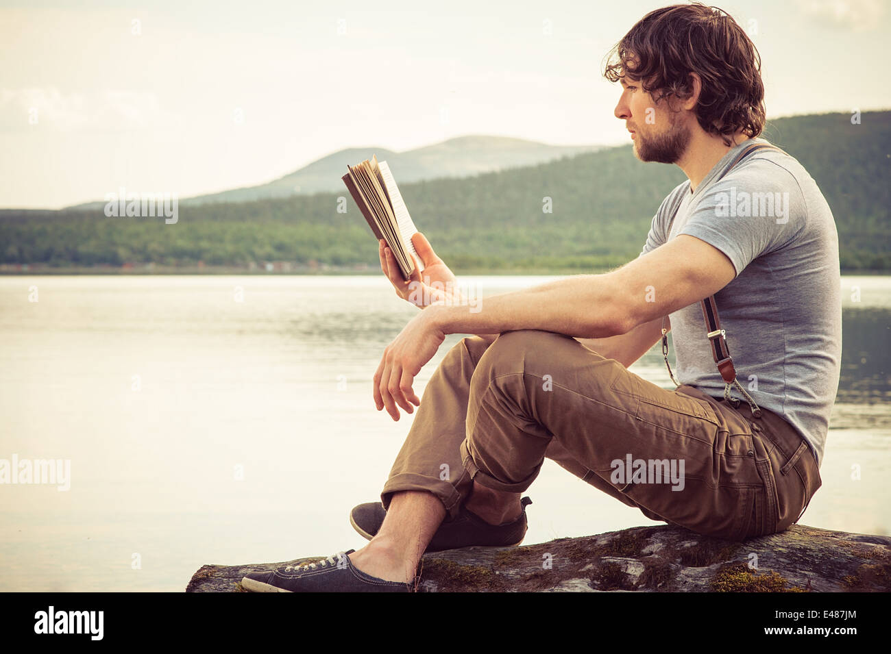 Young Man reading book outdoor with lake on background Summer vacations ...