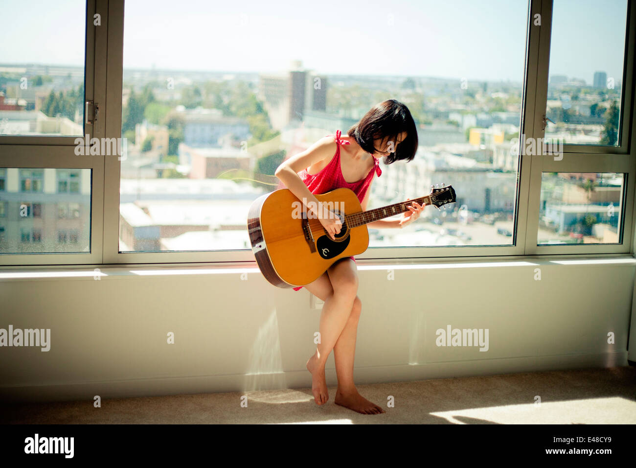 Young woman sitting on window sill and playing guitar Stock Photo - Alamy