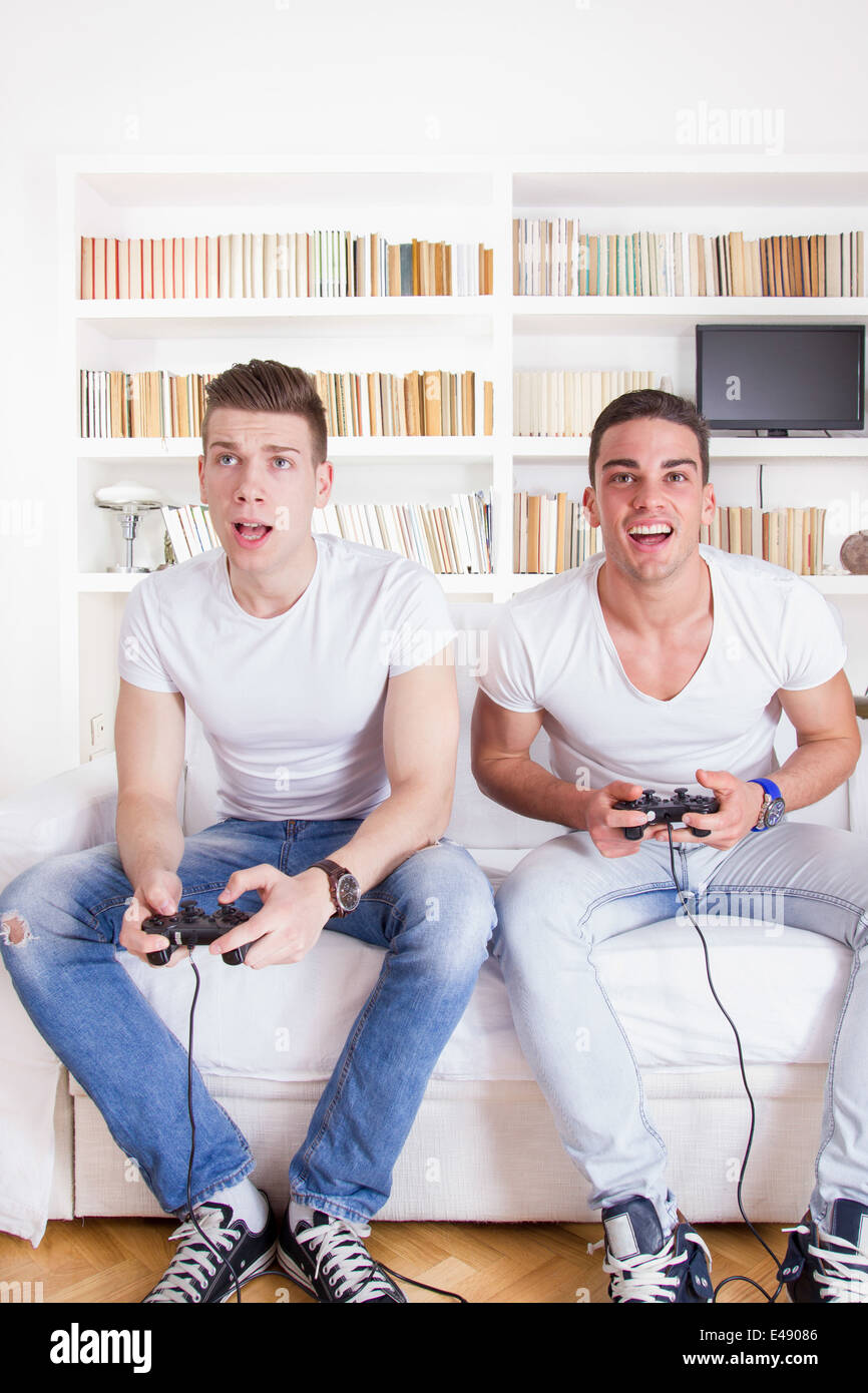two competitive friends at home playing video games with controllers ...