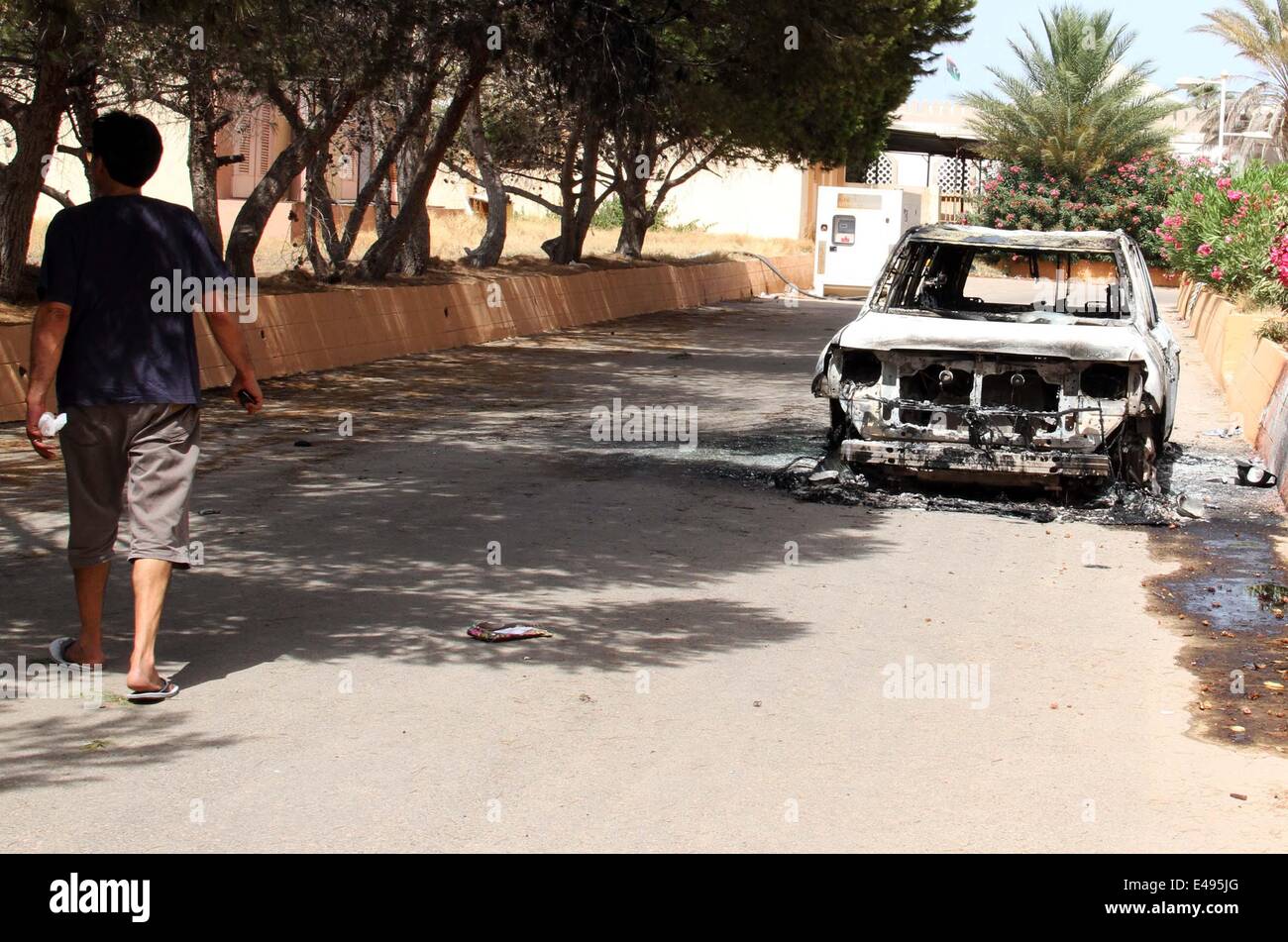 Tripoli, Libya. 6th July, 2014. A journalist walks pass a damaged car ...