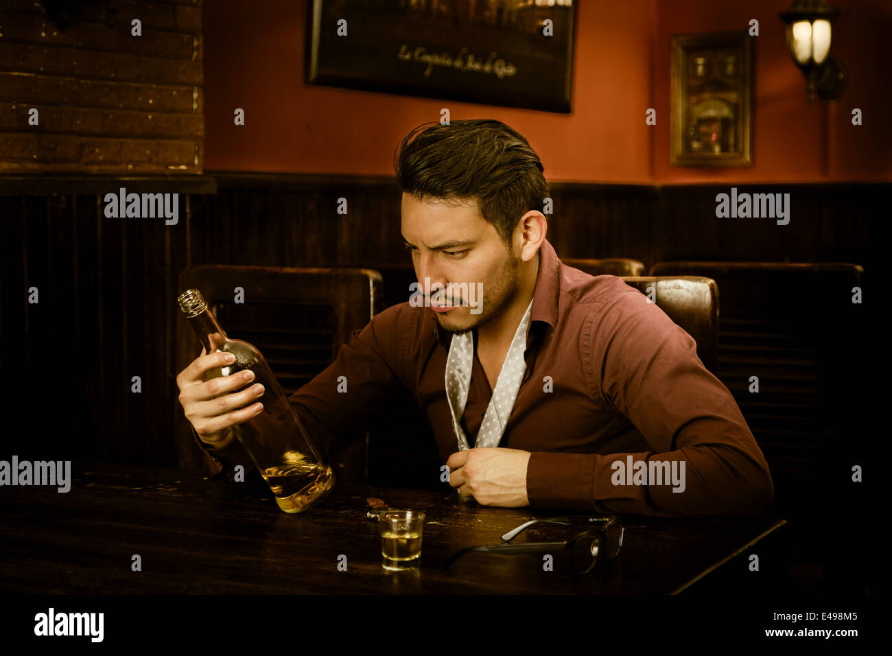 latin guy drinking shots staring at bottle Stock Photo - Alamy