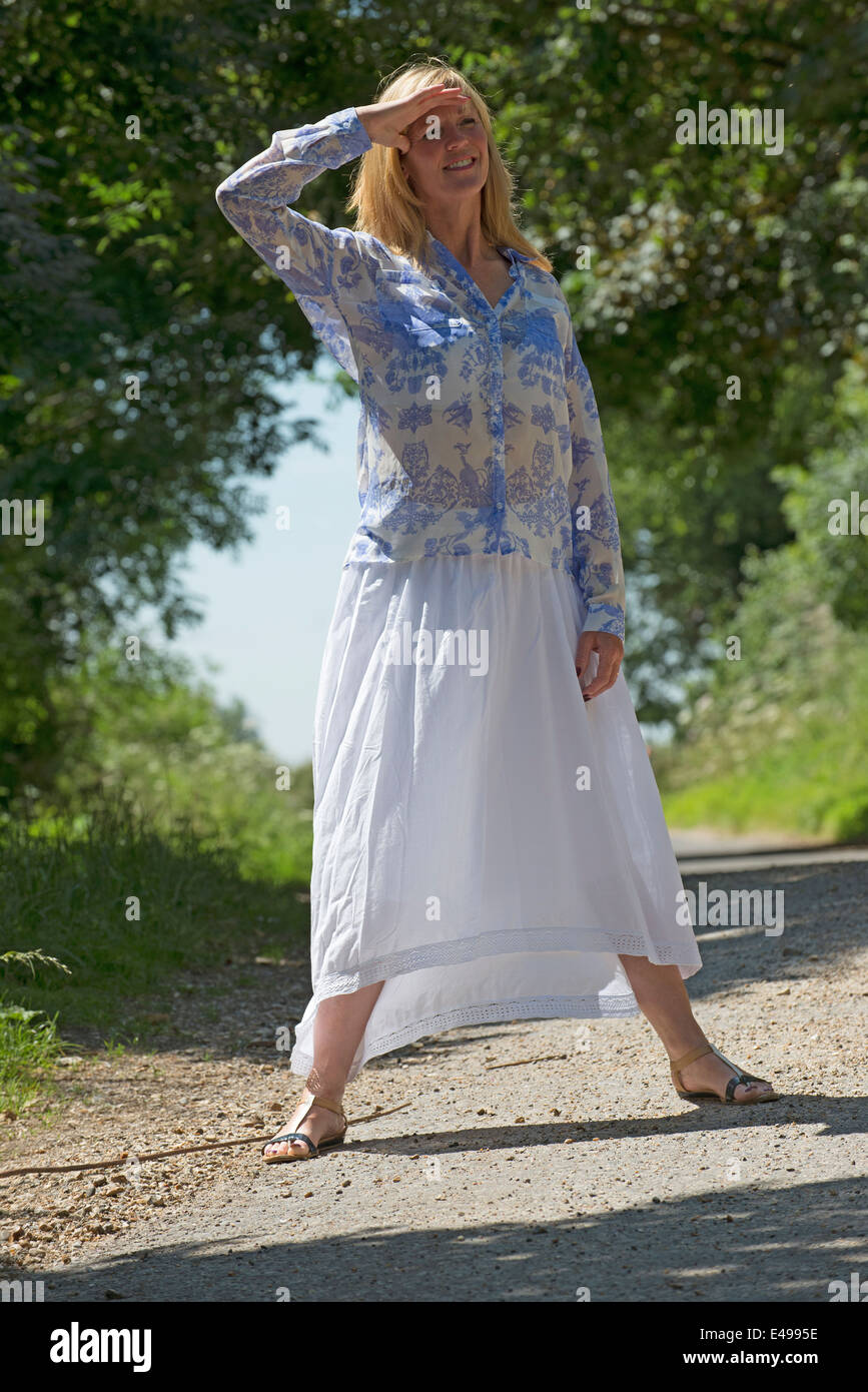 Woman walking in country Lane wearing blue and white outfit Stock Photo ...
