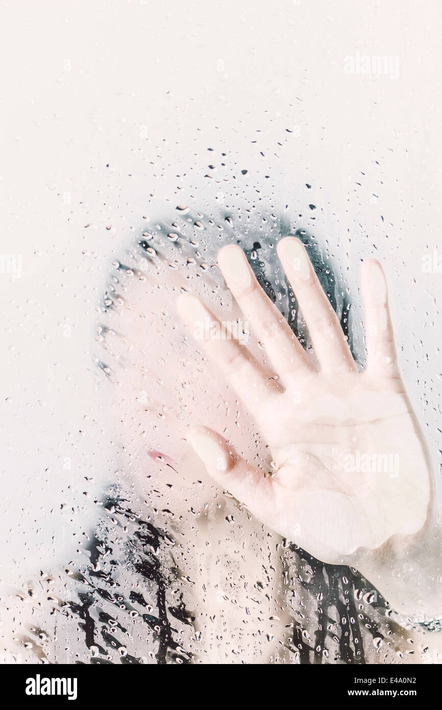 Asian woman behind window pressing hand against pane with water drops ...