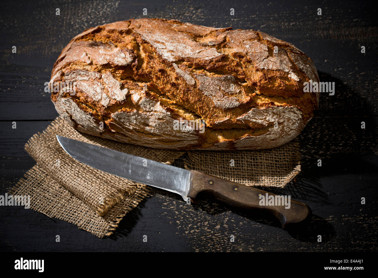 Crusty bread and knife on jute in front of dark background, elevated ...