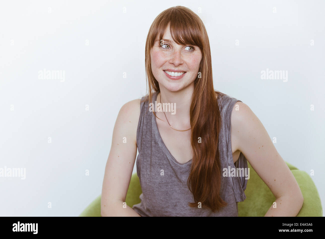 Portrait of smiling woman sitting on soft chair in front of white ...