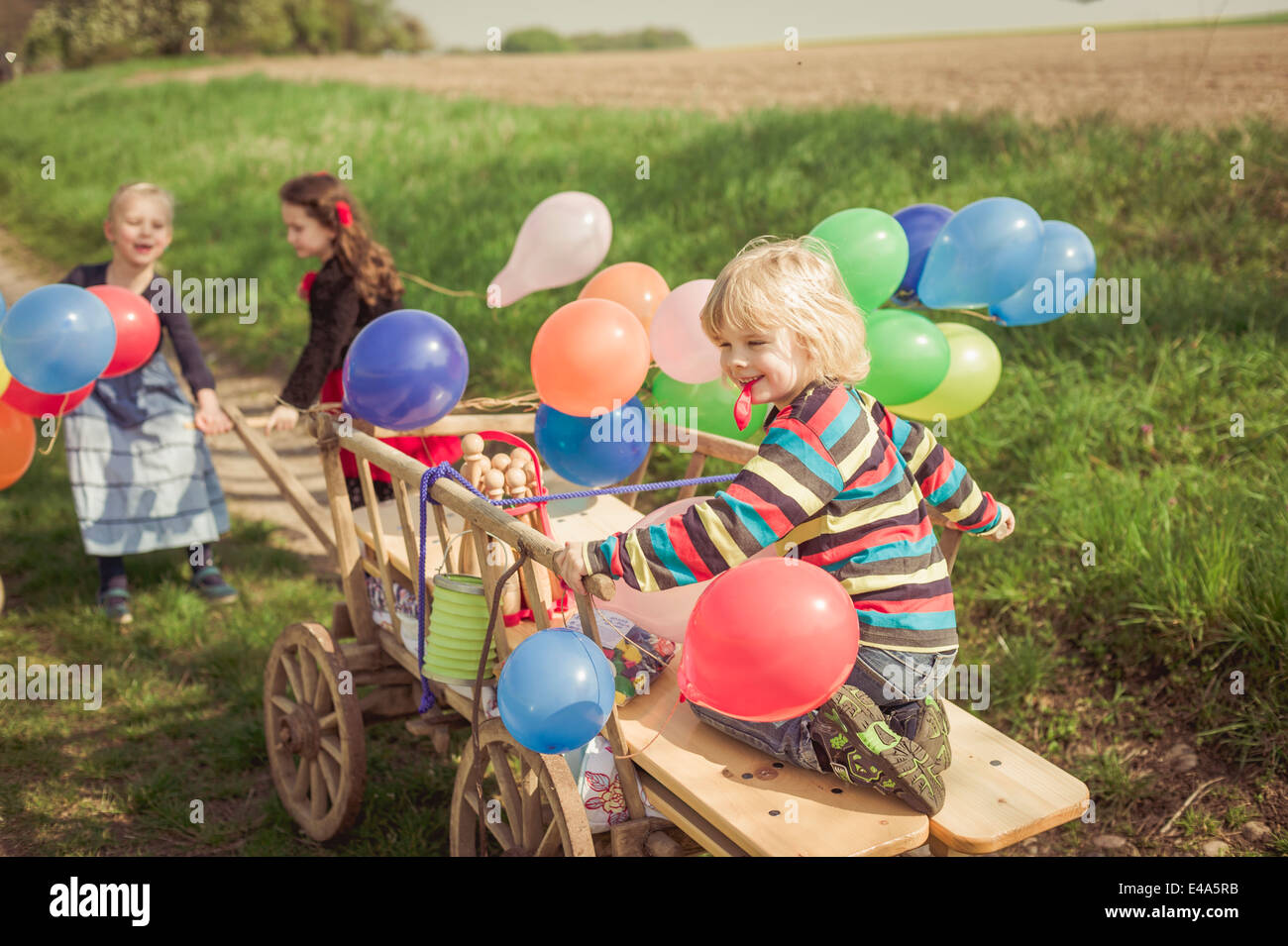 Three children on the move with wooden trolley and balloons Stock Photo ...