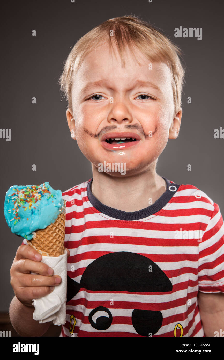 Portrait of crying looking little boy with painted beard and ice cream ...