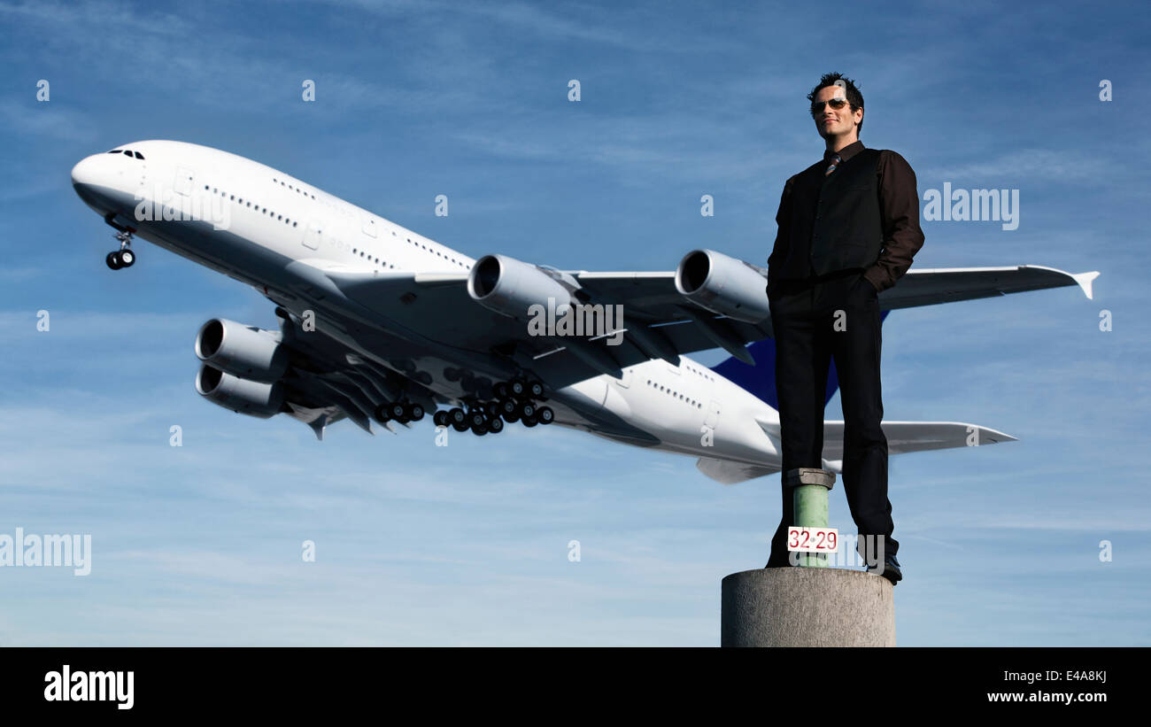 Germany, Mid adult man with airplane in background standing on pillar ...