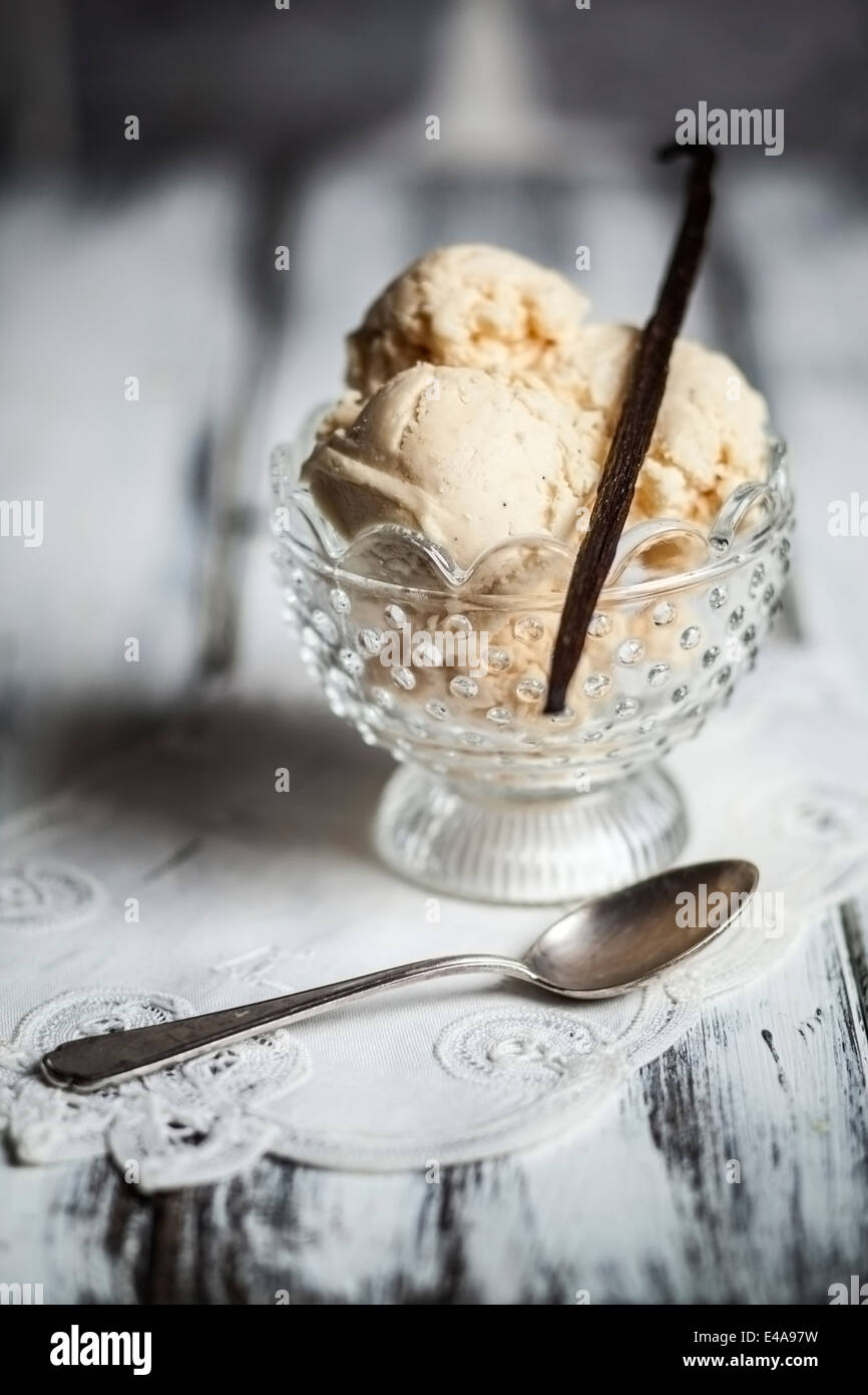 Glass of vanilla ice cream with vanilla pod and spoon on wooden table ...