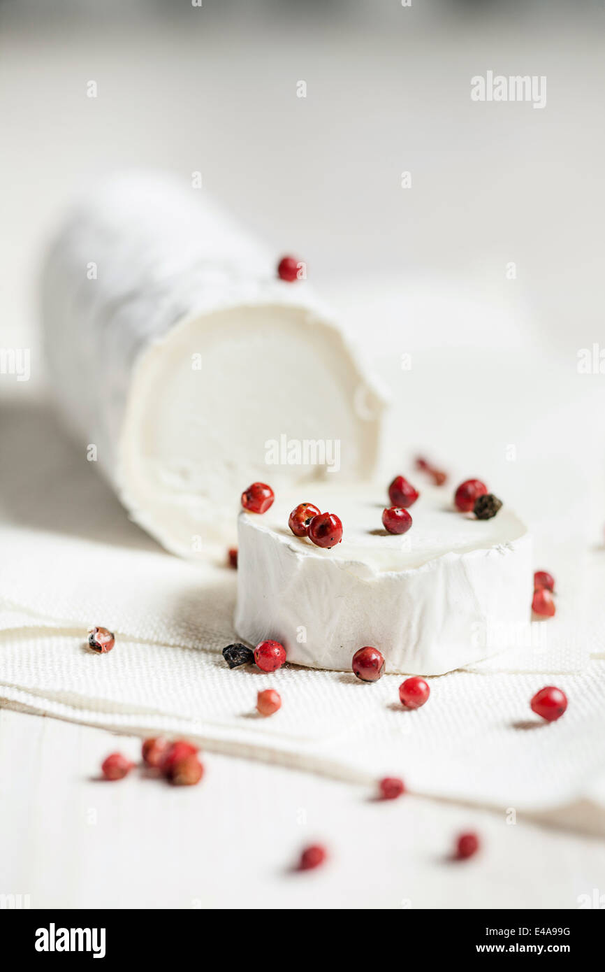 Roll of goat's cheese camembert with red peppercorns on white cloth ...