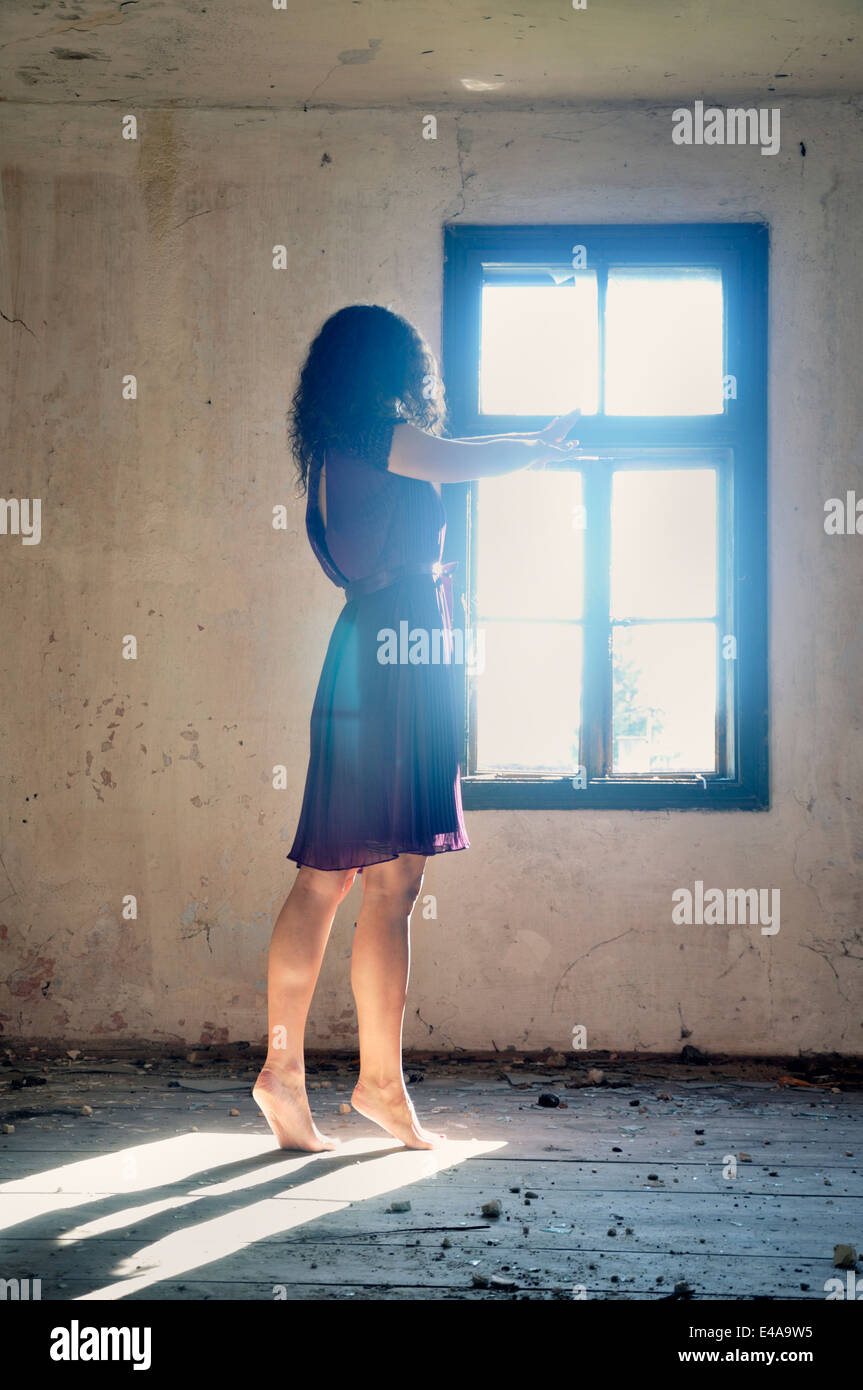 Young woman standing by the window reaching for the light Stock Photo ...