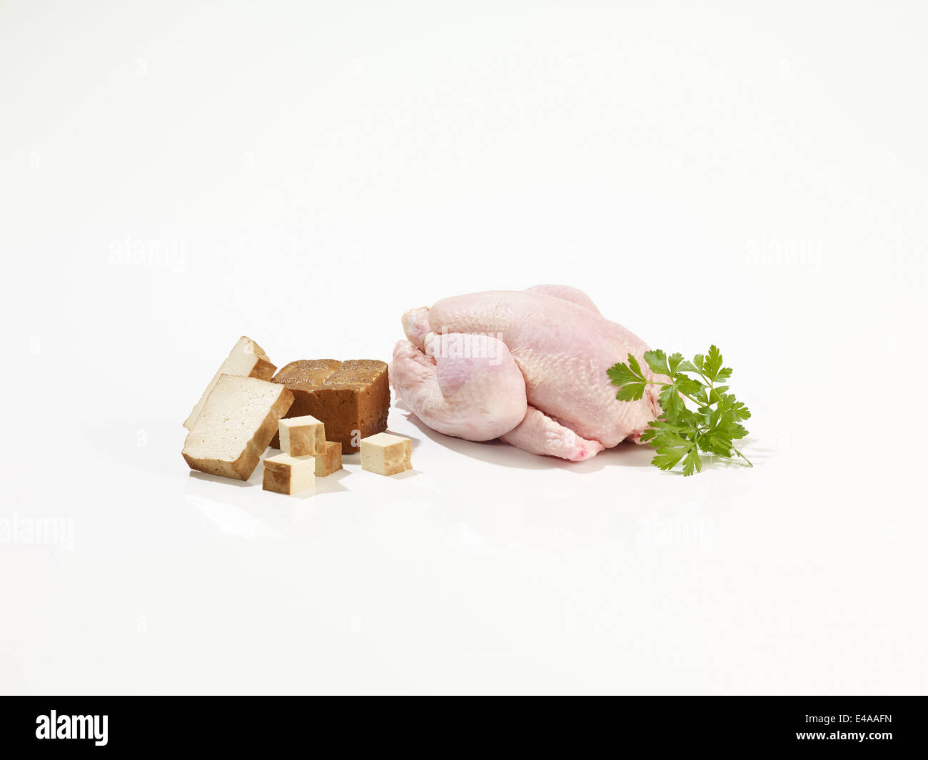Raw boiling fowl, smoked tofu and flat leaf parsley in front of white ...