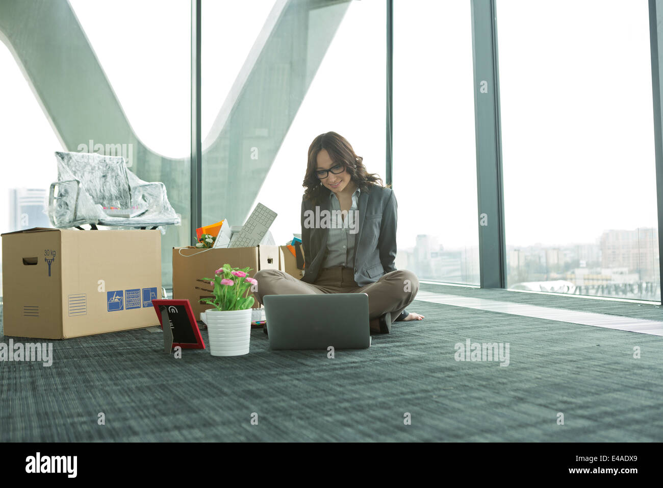 Businesswoman using laptop on empty office floor with cardboard boxes ...