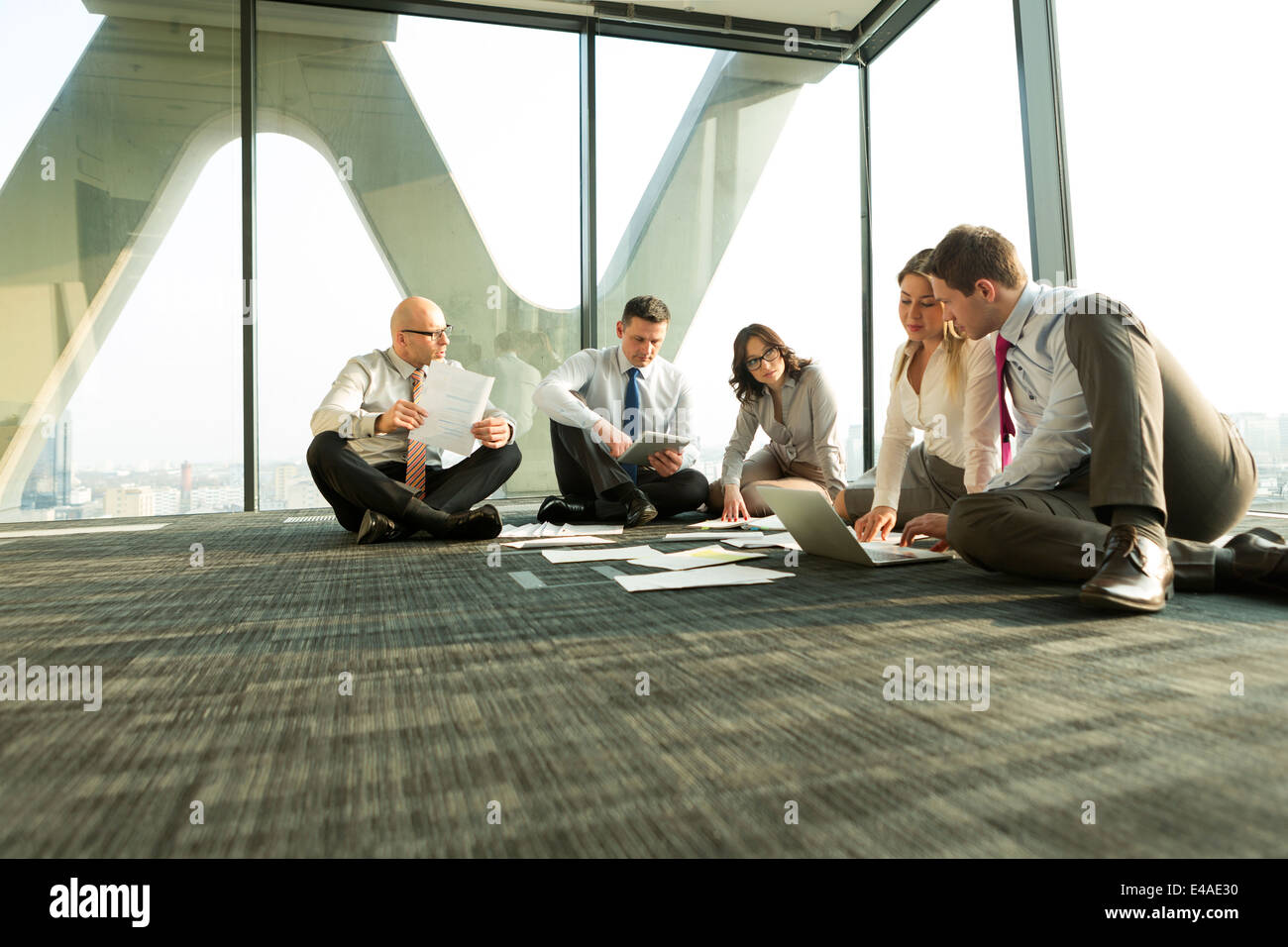 Businesspeople sitting on floor discussing papers Stock Photo - Alamy