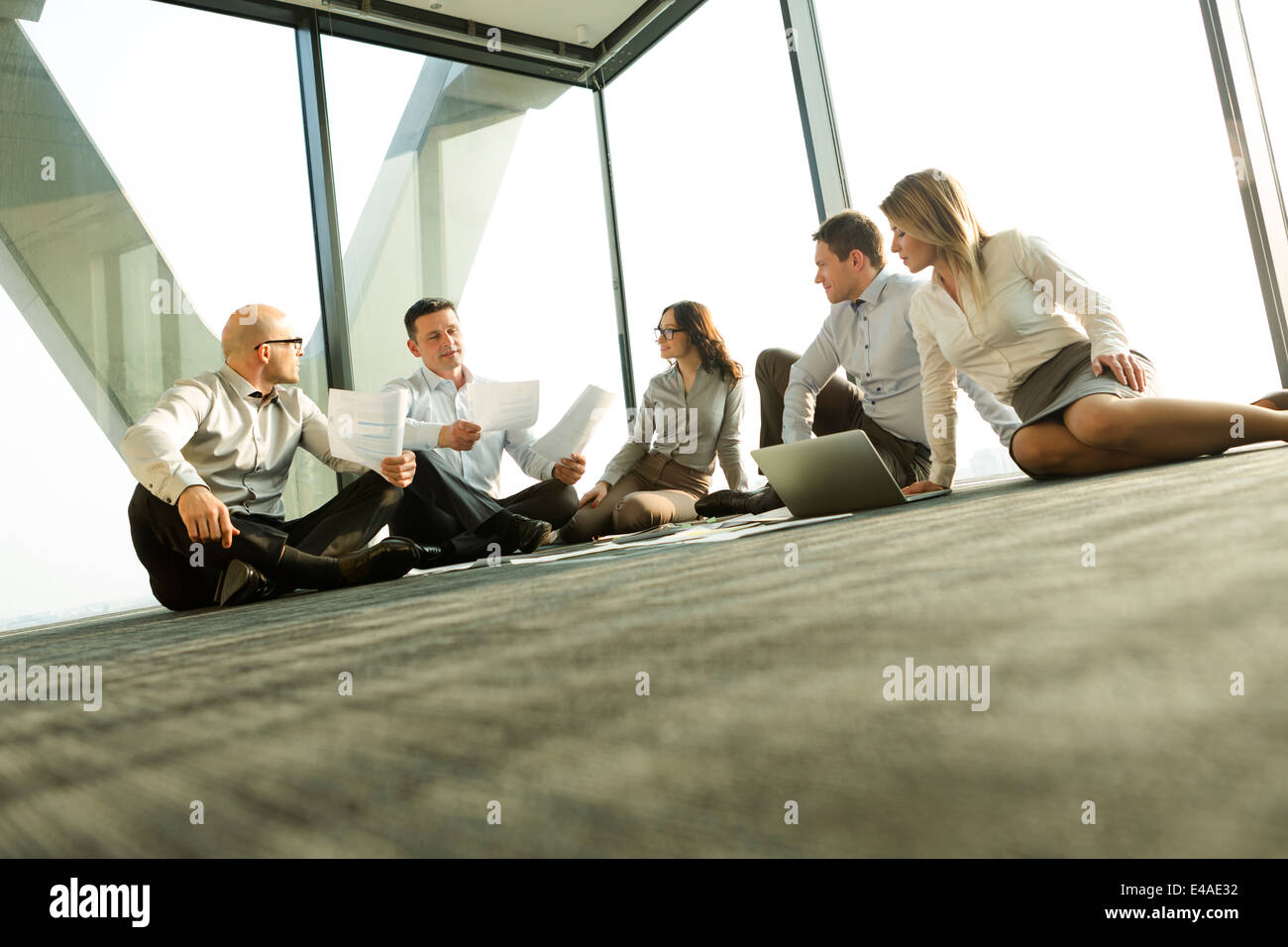 Businesspeople sitting on floor discussing papers Stock Photo - Alamy