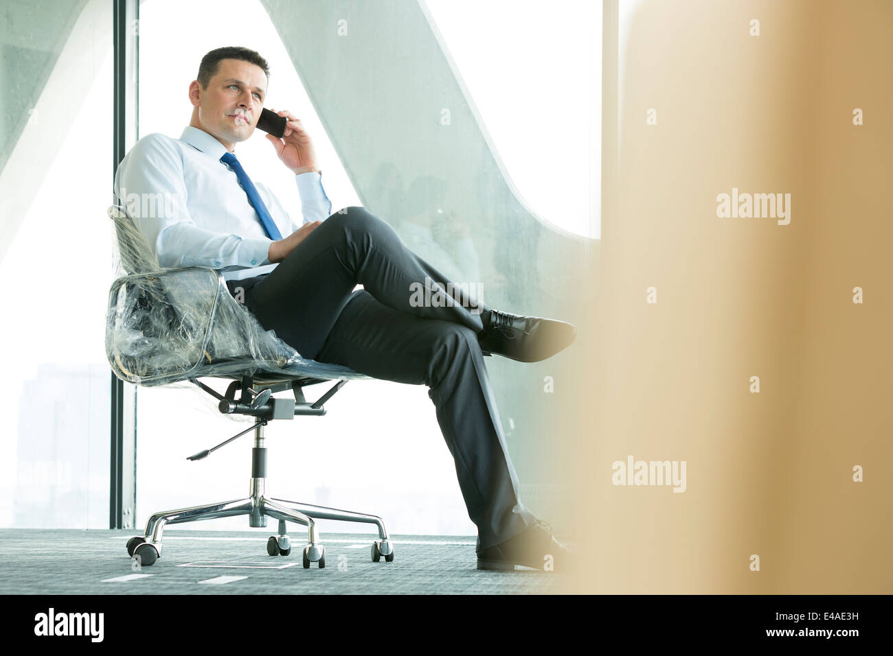 Businessman using cell phone on wrapped office chair Stock Photo - Alamy