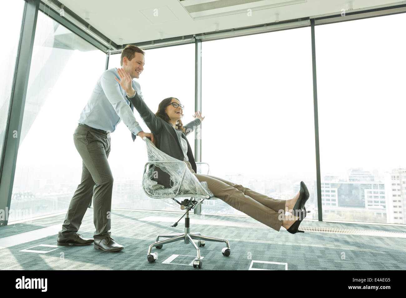 Businessman pushing businesswoman in office chair Stock Photo - Alamy