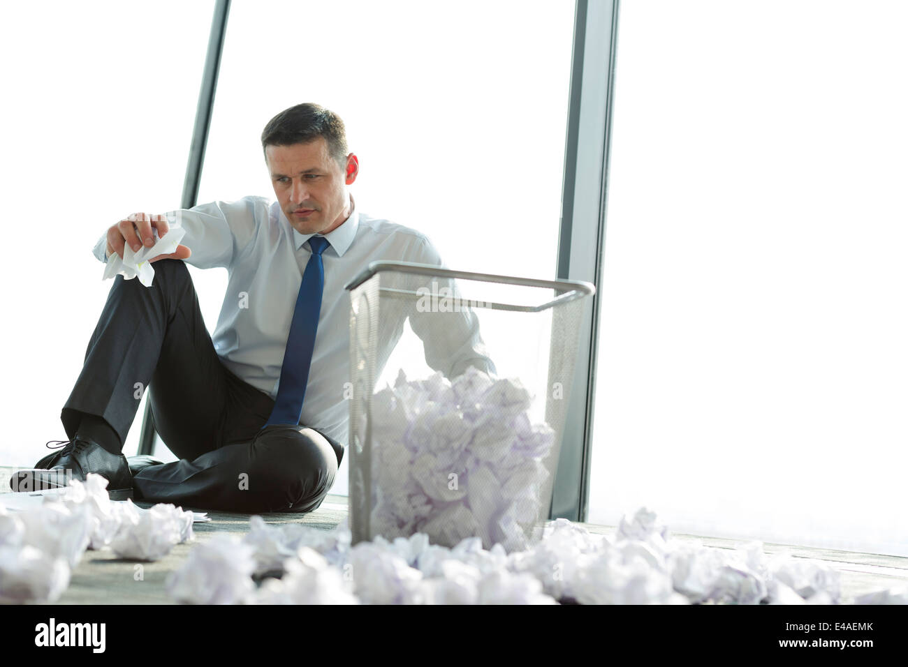 Businessman sitting on office floor surrounded by crumpled paper Stock ...
