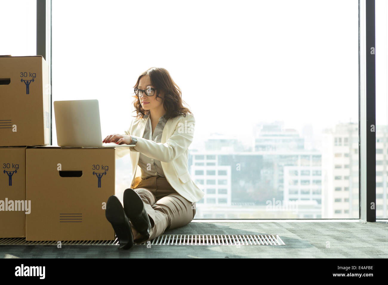 Businesswoman using laptop on empty office floor with cardboard boxes ...