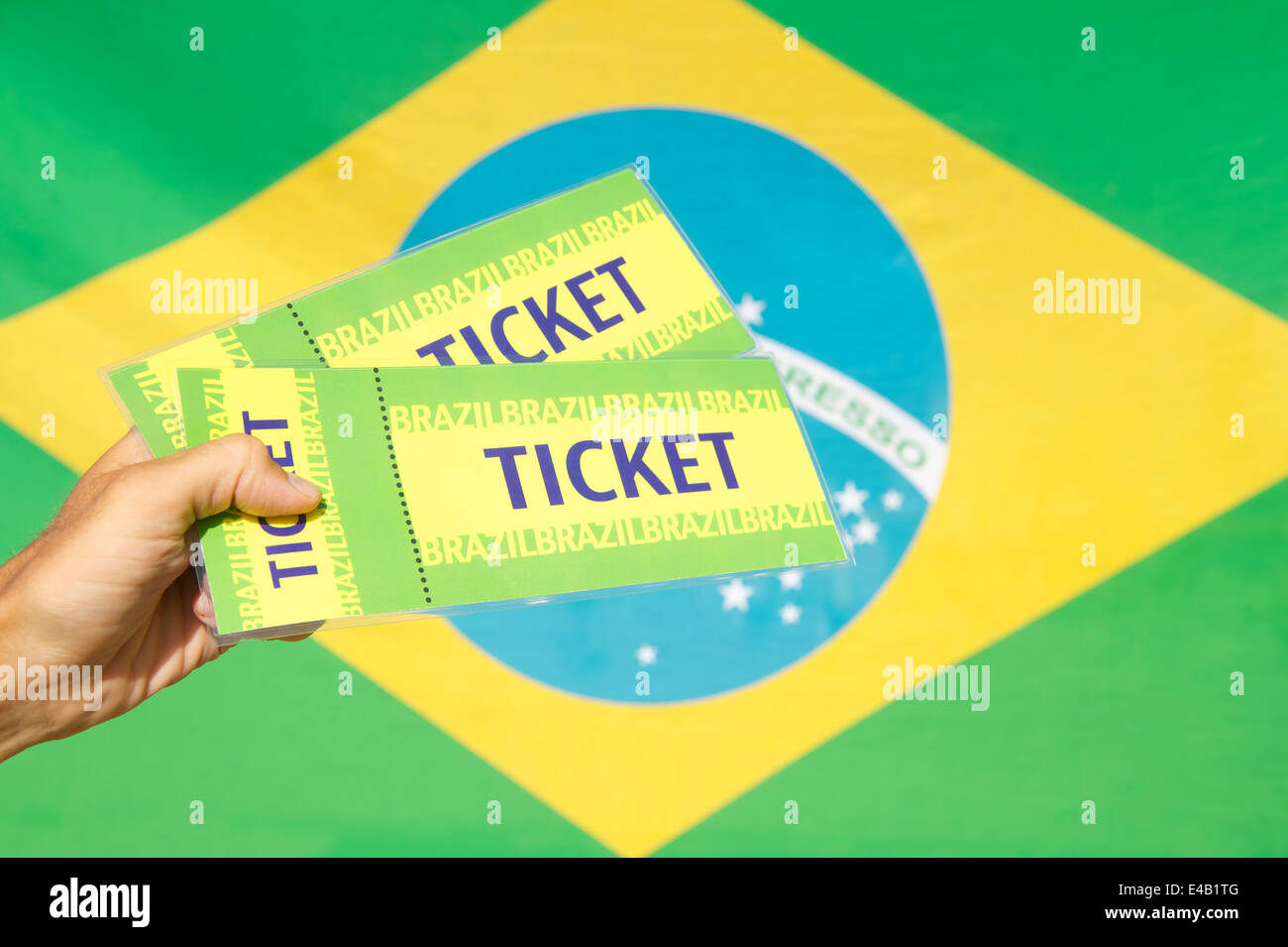 Hand holding two Brazil tickets against bright Brazilian flag ...