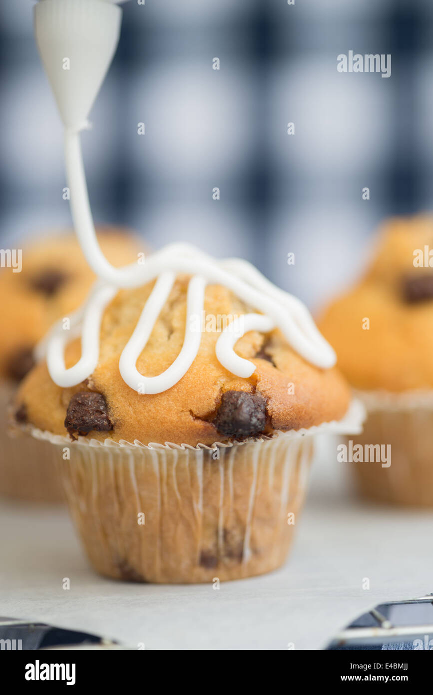Home made chocolate chip muffins with icing frosting being applied ...