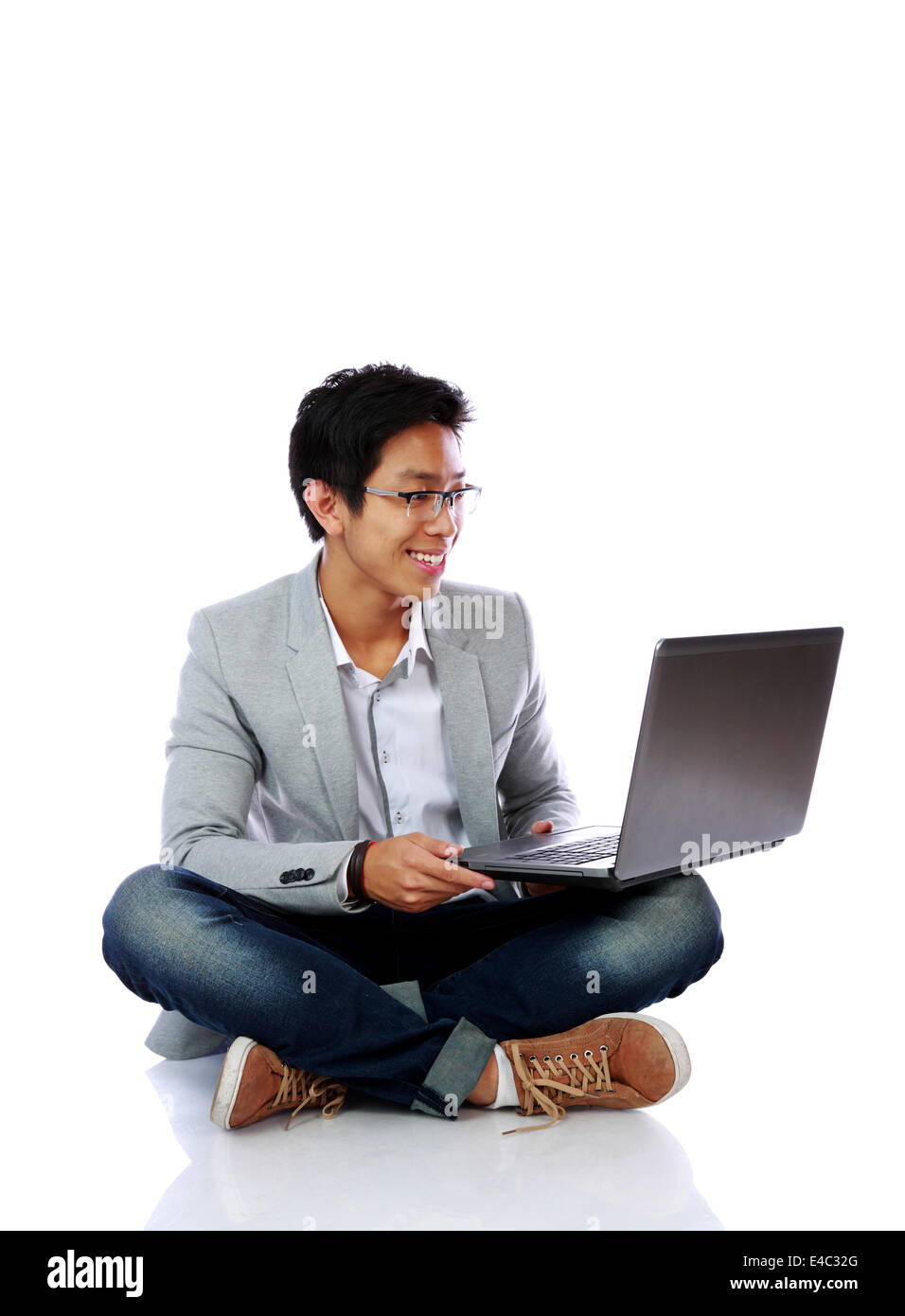 SMiling asian man sitting on the floor and using laptop over white ...