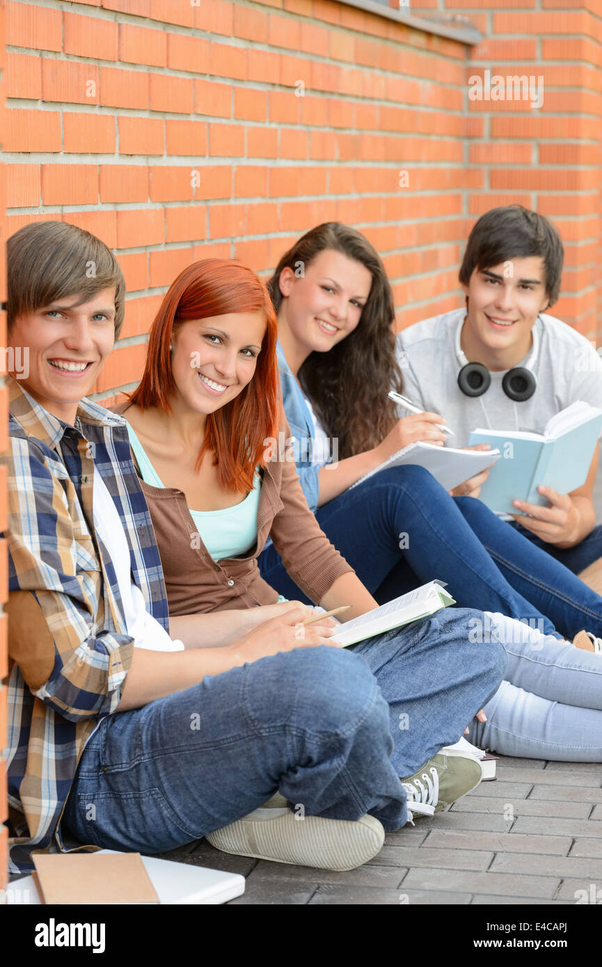 College students sitting on ground against brick wall holding books ...