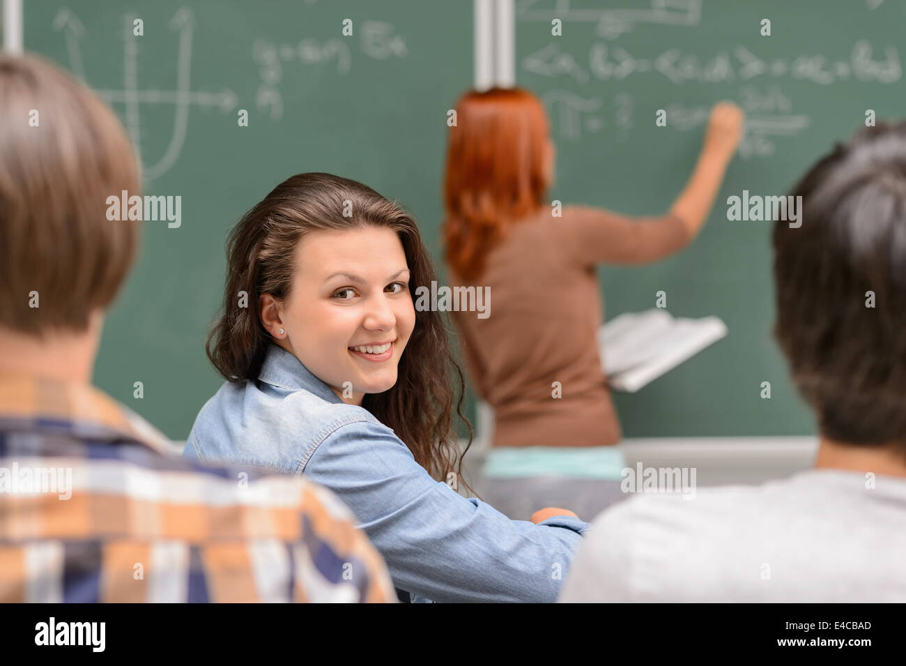 Smiling student girl sitting front of chalkboard during mathematics ...