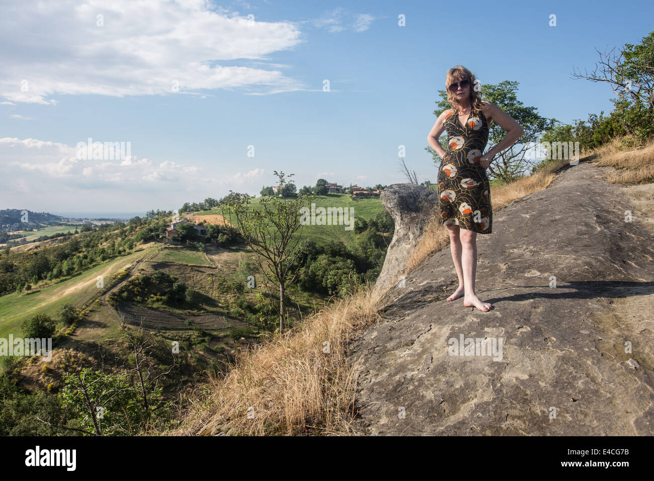 blonde woman wearing dress standing on rock looking out in countryside ...