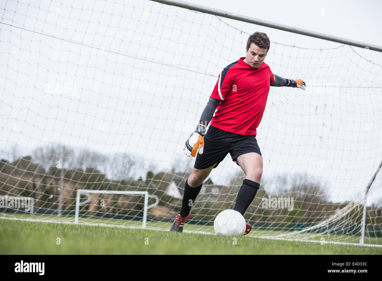 Goalkeeper in red kicking ball away from goal Stock Photo - Alamy