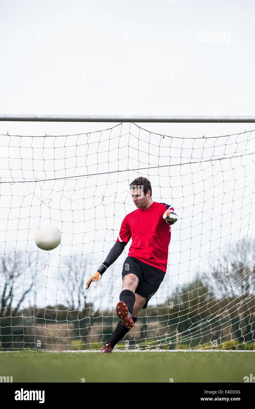 Goalkeeper in red kicking ball away from goal Stock Photo - Alamy
