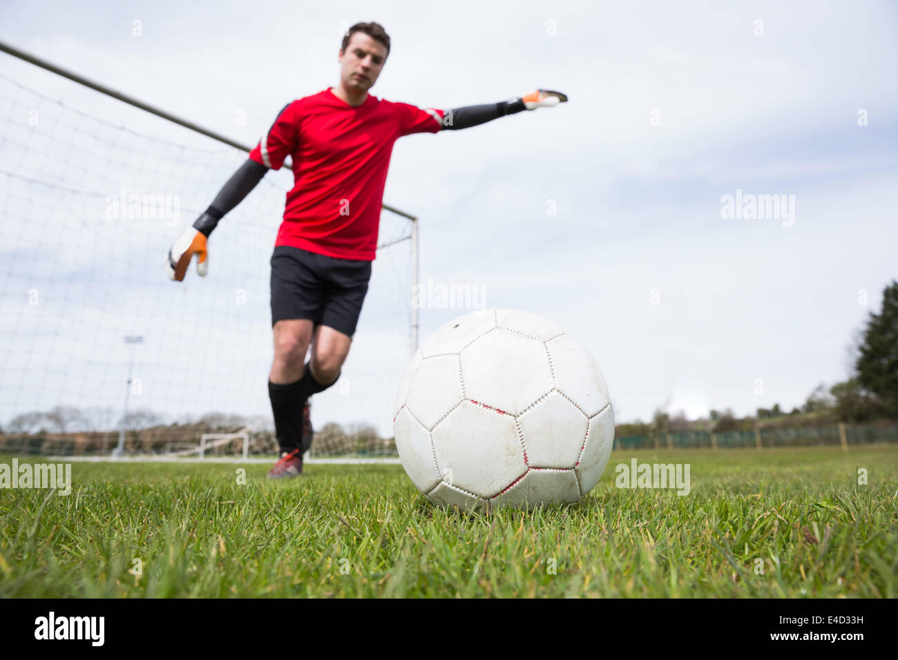 Goalkeeper in red kicking ball away from goal Stock Photo - Alamy