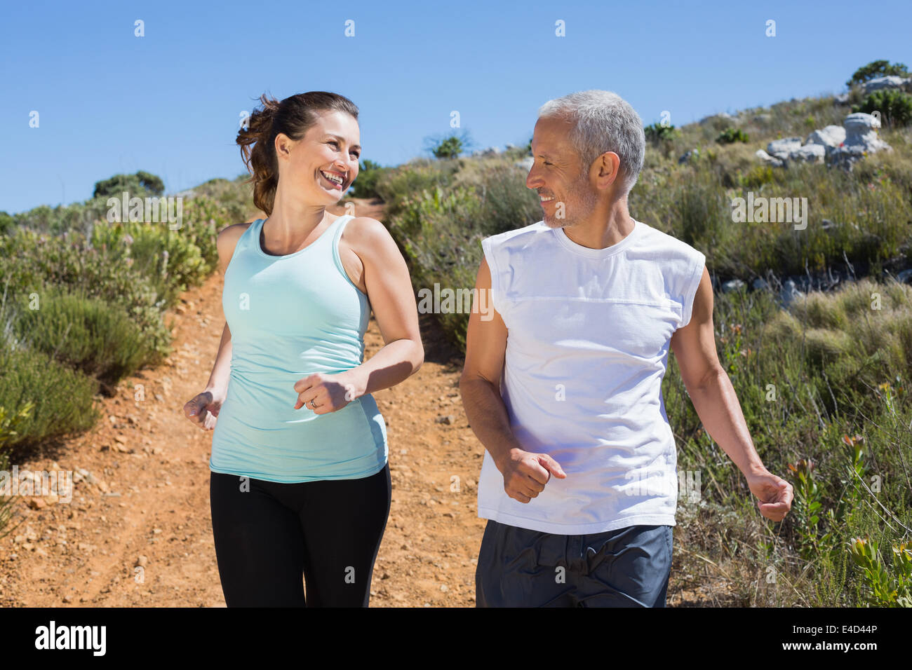 Fit smiling couple jogging down mountain trail Stock Photo - Alamy