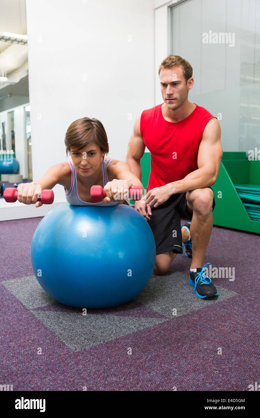 Personal trainer with client lifting dumbbells on exercise ball Stock ...