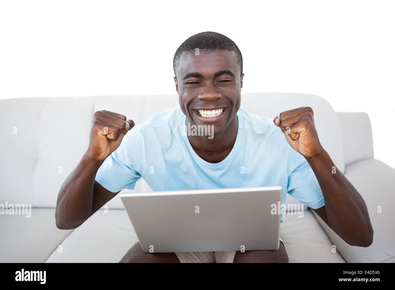 Cheering man sitting on couch using laptop Stock Photo - Alamy