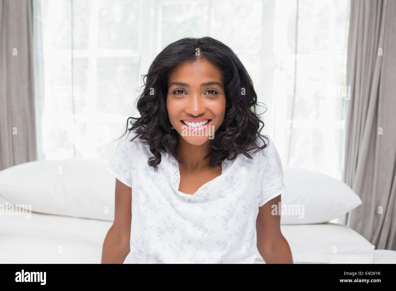 Pretty woman smiling at camera sitting on bed Stock Photo - Alamy
