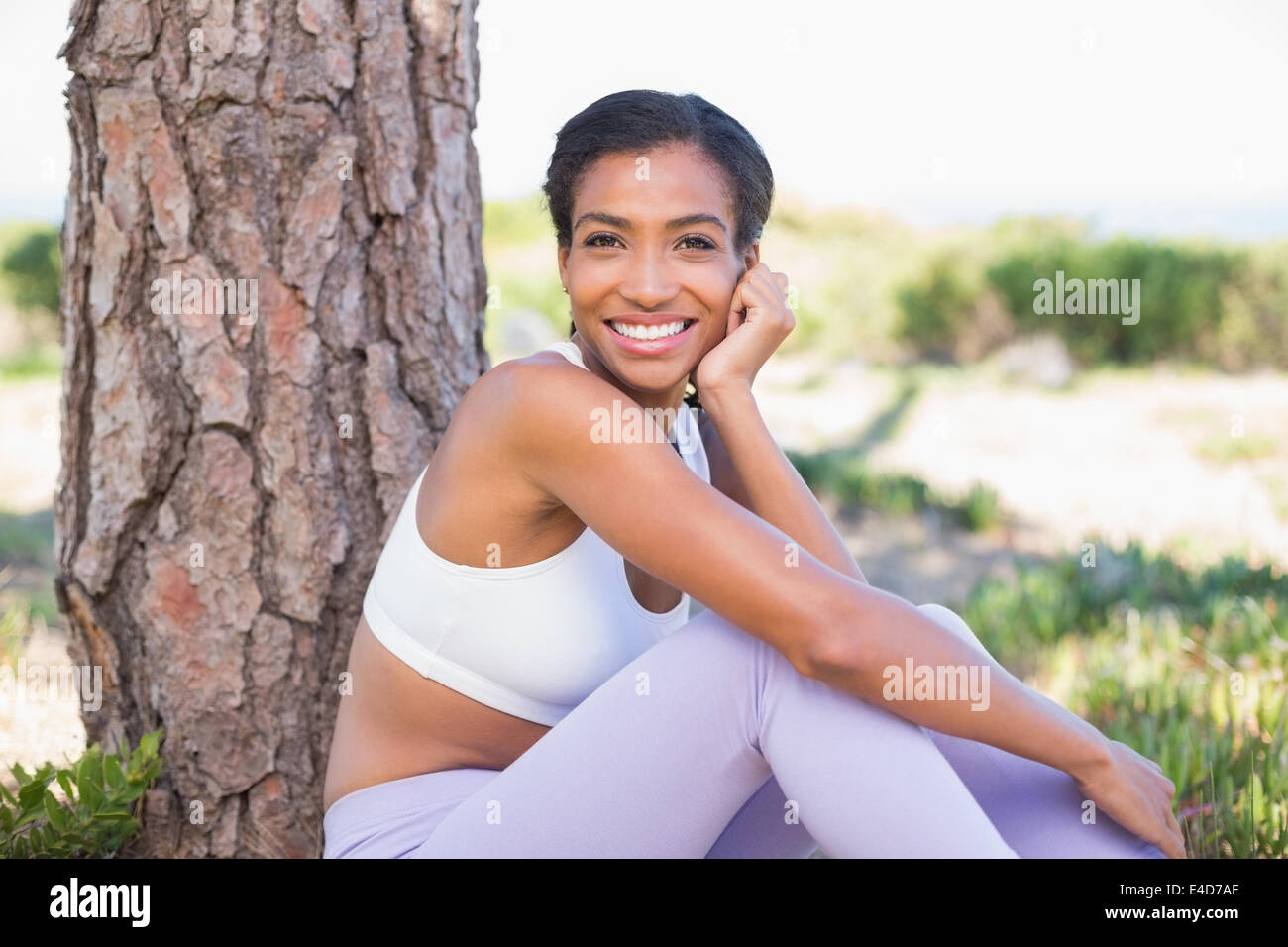Fit woman sitting against tree smiling at camera Stock Photo - Alamy