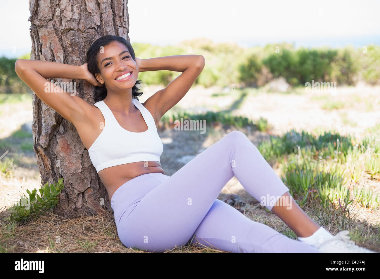 Fit woman sitting against tree smiling at camera Stock Photo - Alamy